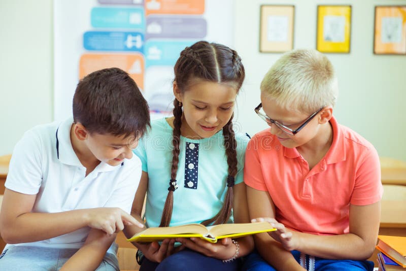 Happy Elementary School Students Sitting on Desk and Reading a Book at ...