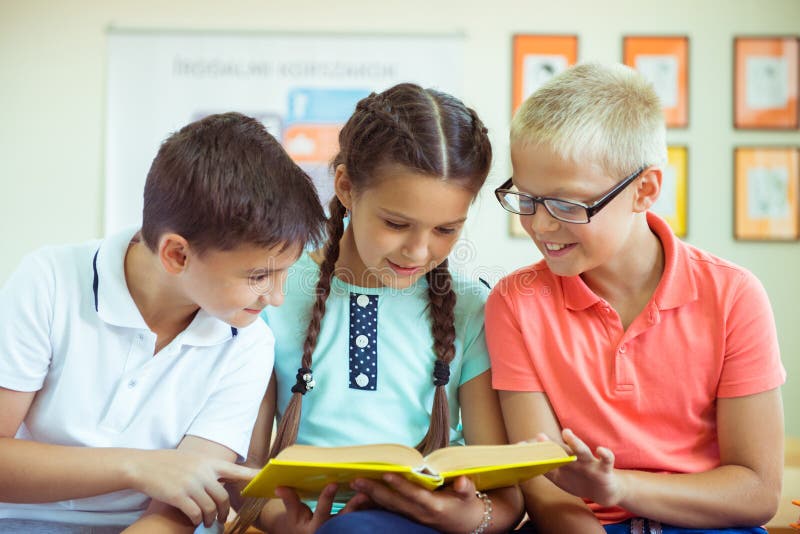 Happy Elementary Students Sitting on Desk with Book and Discussing in ...