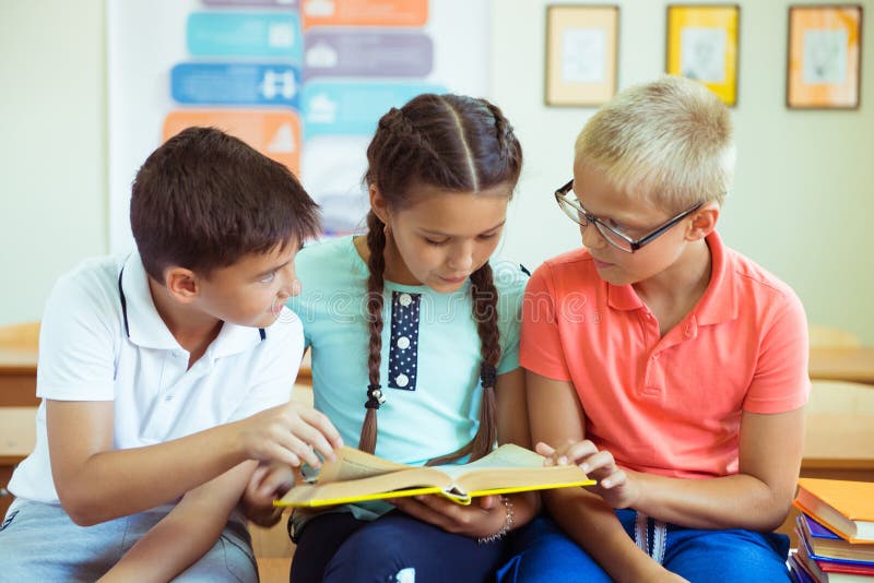 Happy Elementary Students Sitting on Desk with Book and Discussing in ...