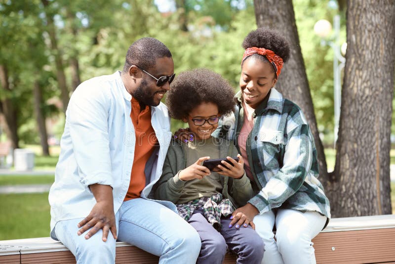Happy Family with Smartphone Communicating through Video Chat in Park ...
