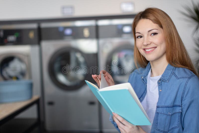 Happy Female Reading Book while Doing Washing in Laundromat Stock Photo ...