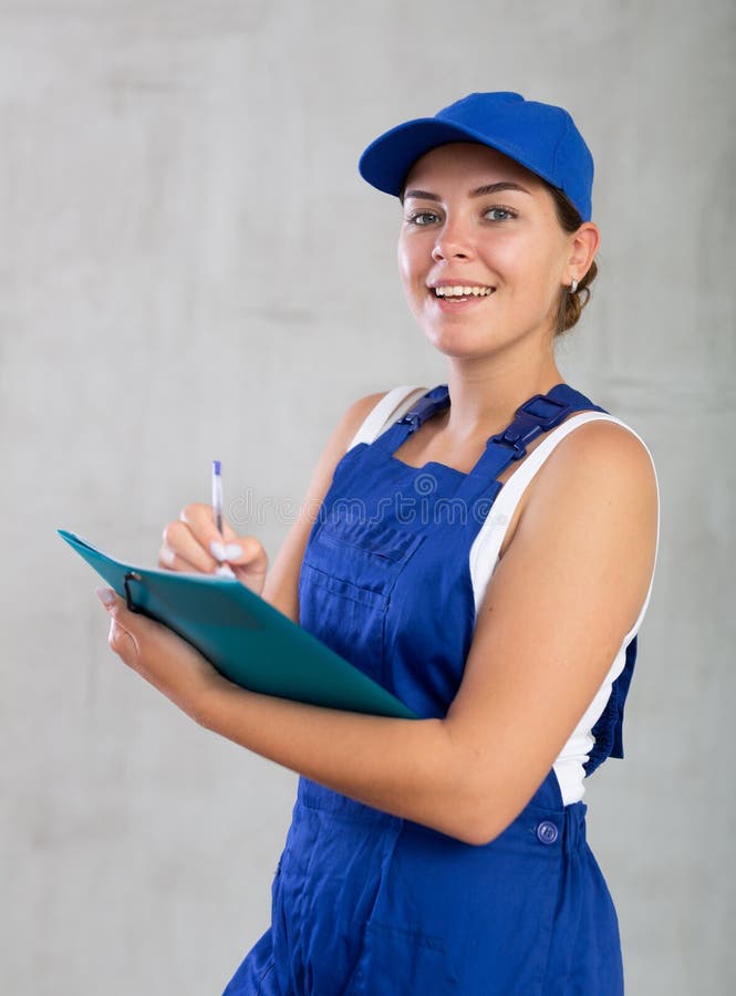 Happy Female Worker in Work Clothes Making Notes in File with Papers ...