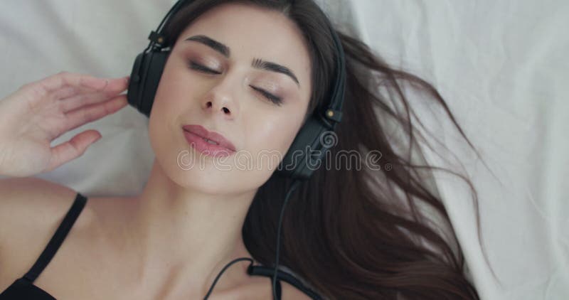 Happy Girl Listening To Music On Bed Flirts At Camera Twists Headphones Wire Stock Footage