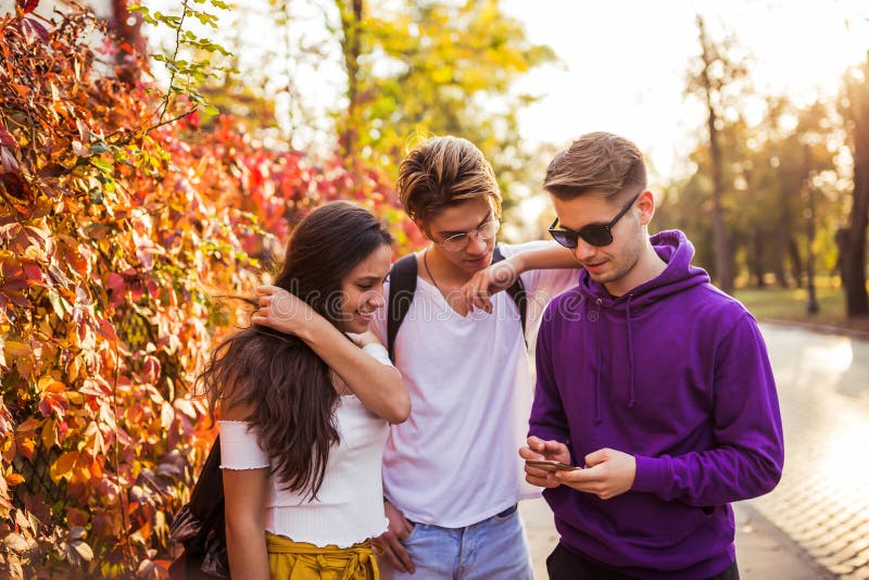 Happy Group of Three Friends Using a Smart Phone Standing Outdoors ...