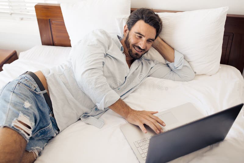 Happy Handsome Man Using Laptop. Lying on Bed in Bedroom. Stock Image ...