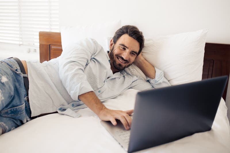 Happy Handsome Man Using Laptop. Lying on Bed in Bedroom. Stock Photo ...
