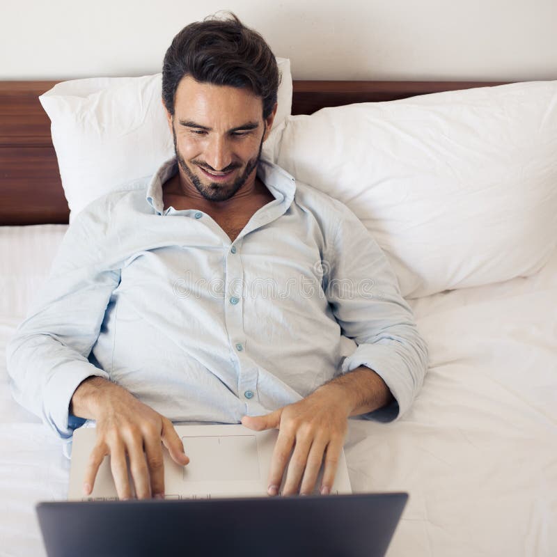 Happy Handsome Man Using Laptop. Lying on Bed in Bedroom. Stock Photo ...