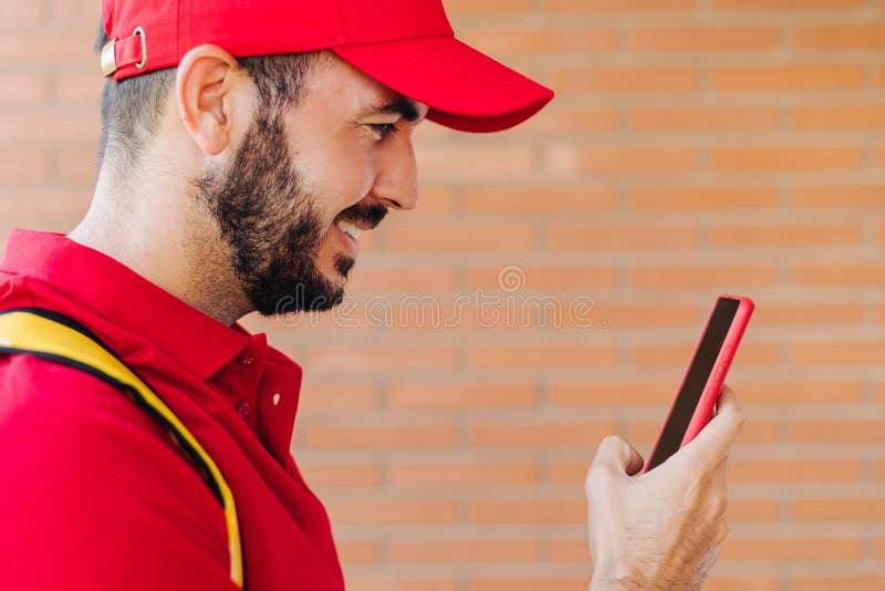 Happy Hispanic Delivery Man in Red Clothes Using Mobile Phone Stock ...
