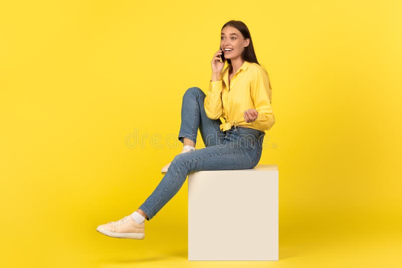 Happy Lady Talking on Cellphone Sitting on Cube, Yellow Background ...