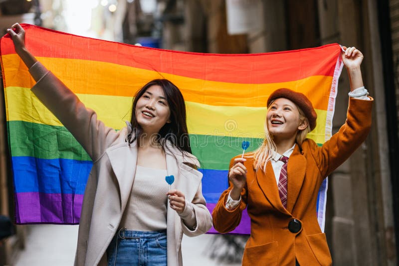 Happy Lesbian Couple Holding A Rainbow Flag While Walking Outdoors