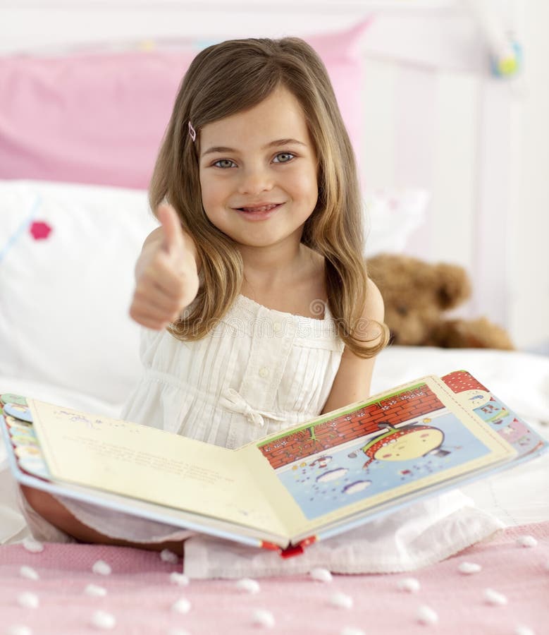 Happy Little Girl Reading in Bed with Thumb Up Stock Photo - Image of ...