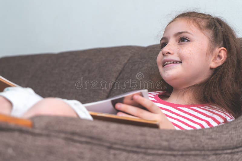 Happy Little Girl Reading Book on Sofa Stock Image - Image of portrait ...