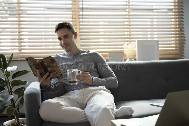 Man in Casual Clothes Reading Book and Drinking Coffee on Sofa. Stock ...