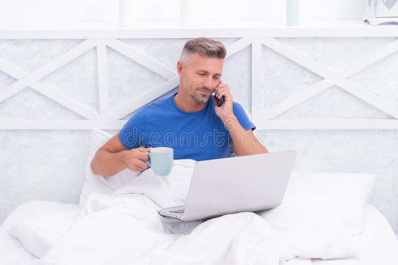 Happy Man Talk on Mobile Phone Drinking Coffee and Using Laptop in Bed ...