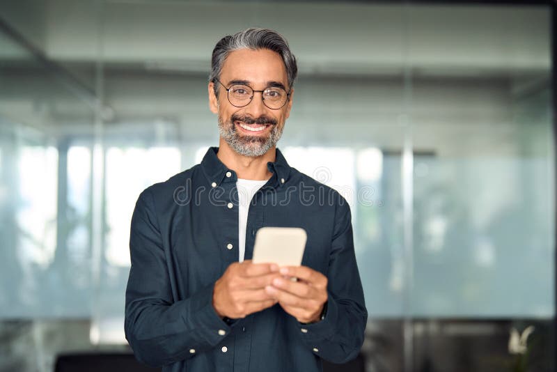 Happy Mature Business Man Wearing Suit Standing In Office Using Mobile