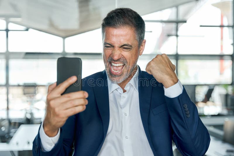 Happy Mature Business Man Wearing Suit Standing In Office Using Mobile