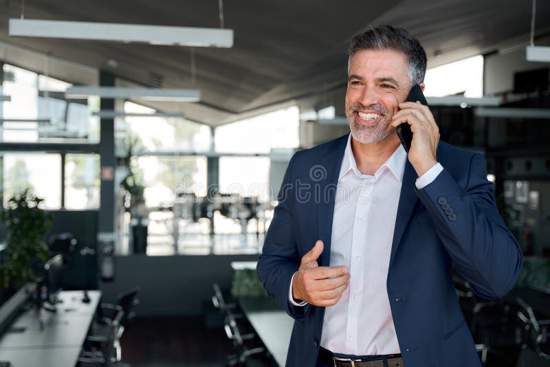 Happy Mature Business Man Wearing Suit Standing In Office Using Mobile