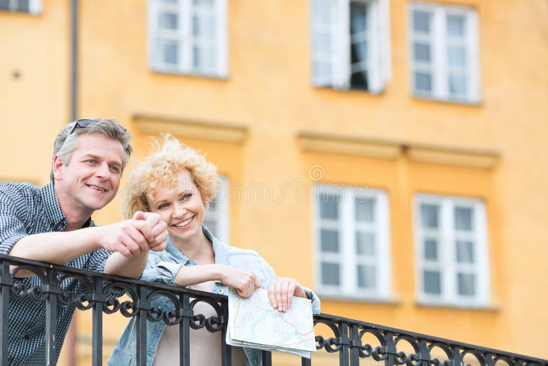Happy Middle-aged Couple with Map Leaning on Railing Against Building ...