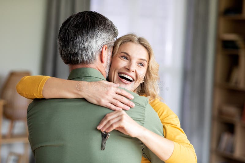 Happy Middle Aged Woman Hugging Husband And Holding Home Keys In Hand