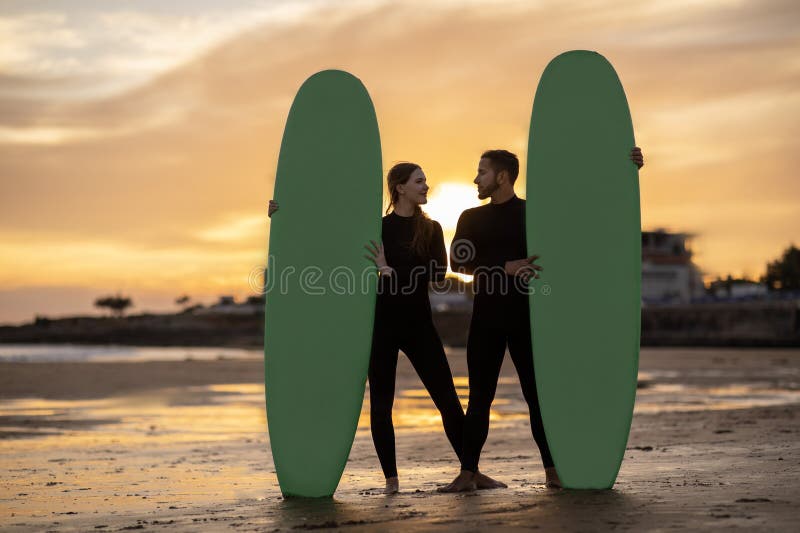 Happy Millennial Couple With Surfboards Standing On The Beach On Sunset