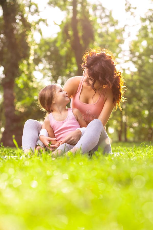 Happy Mother And Daughter Sitting In The Park Together And Looking At