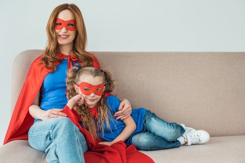 Happy Mother And Daughter In Superhero Costumes Sitting On Sofa And