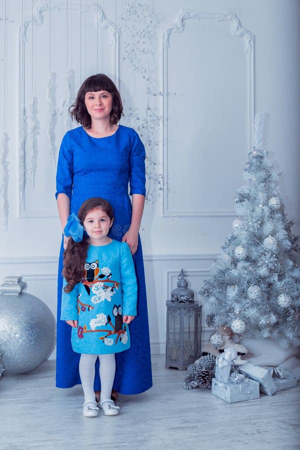 Happy Mother With Her Daughter In Long Blue Dresses Stand Near The