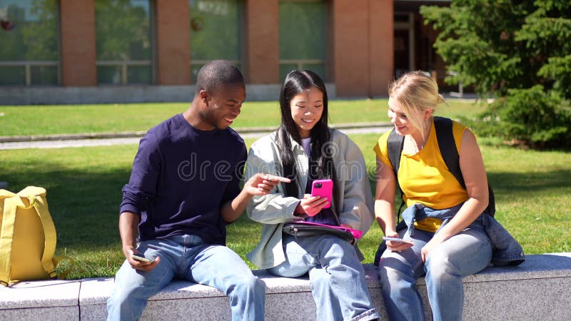 Happy Multi-ethnic Students Using Mobile and Sitting Outside the Campus ...