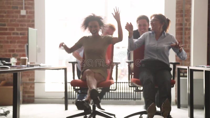 Happy Multicultural Office Workers Laughing Having Fun Riding on Chairs ...