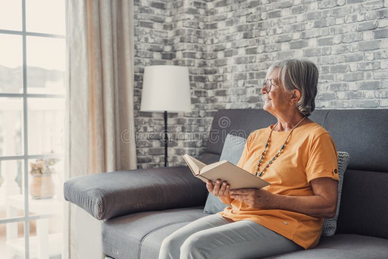Happy Older Blonde Woman Sitting On Comfortable Sofa In Living Room