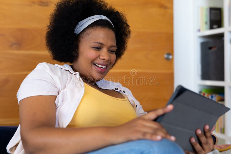 Happy Plus Size African American Woman Sitting On Sofa And Using Tablet