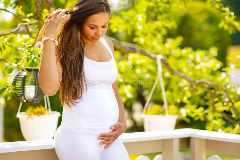 Exhausted Pregnant Woman Standing In Garden Holding Hands On Her Back