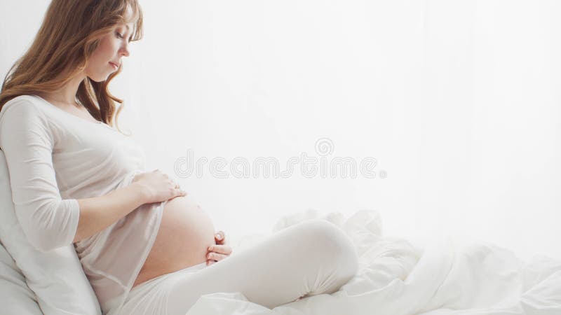 Happy Pregnant Woman Touching Her Beautiful Belly Sitting In The Bed