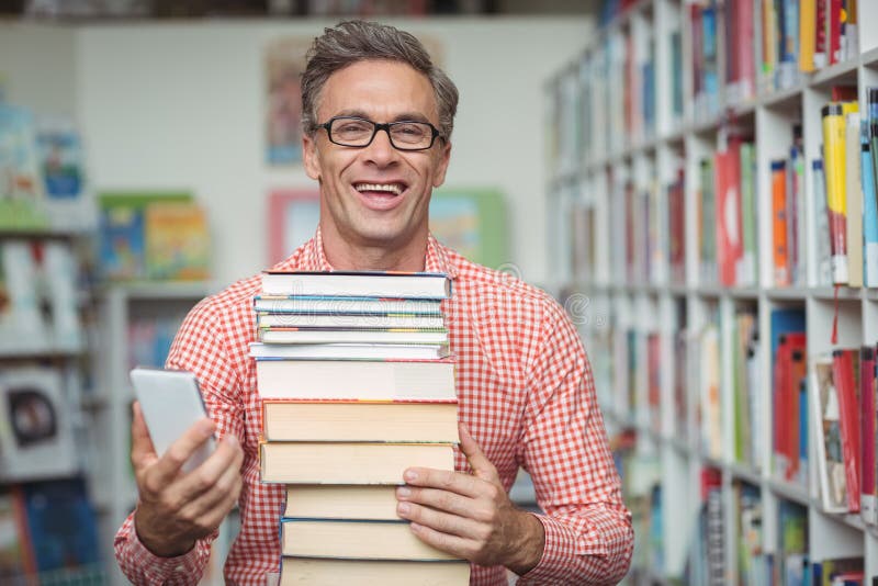 Happy School Teacher Holding Stack of Books while Using Mobile Phone in ...