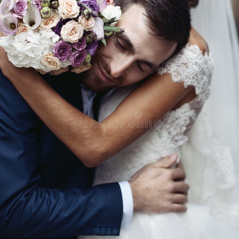Happy Sensual Handsome Groom Hugging Beautiful Bride With Bouquet In
