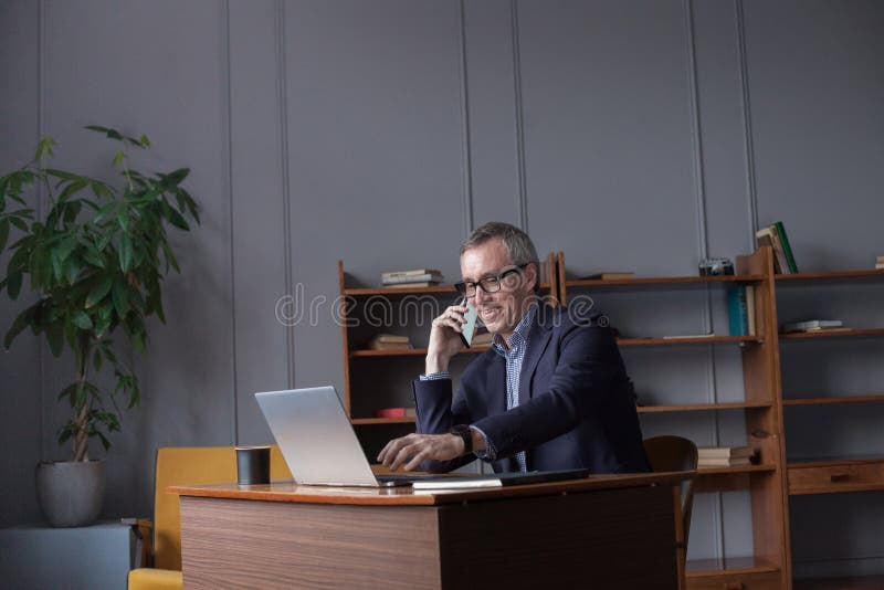Happy Smiling Mature Businessman Talking on Phone while Using Laptop ... Happy Smiling Mature Businessman Talking on Phone while Using Laptop ...