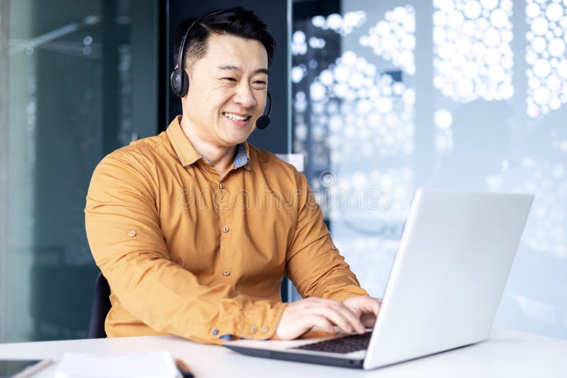 Asian Smiling Young Man Sitting in Office at Desk in Front of Camera ...