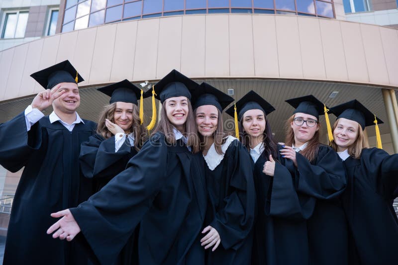 Happy Students in Graduate Gown Stand in a Row Against the Backdrop of ...