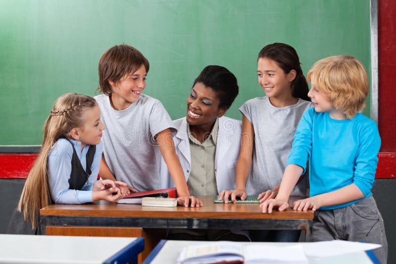 Happy Teacher with Students Communicating at Desk Stock Photo - Image ...