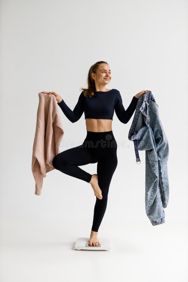 Happy Thin Young Girl With Oversized Clothes In Her Hands On The Scales