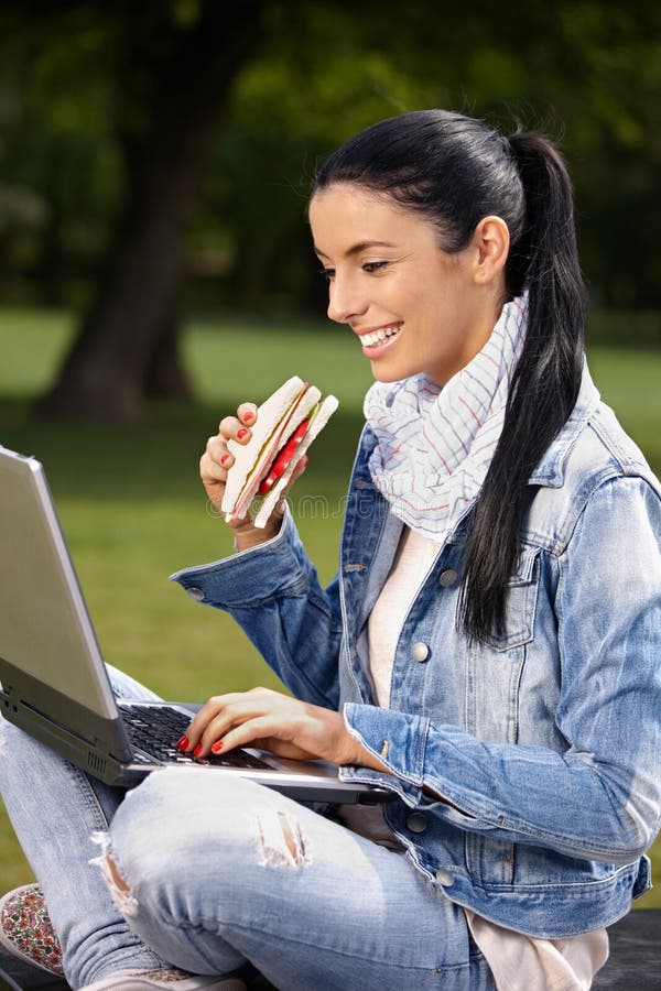Happy Woman Browsing Internet in Park Eating Stock Photo - Image of ...