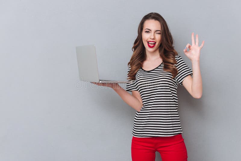 Happy Young Lady Standing Over Grey Wall and Using Laptop Stock Photo ...