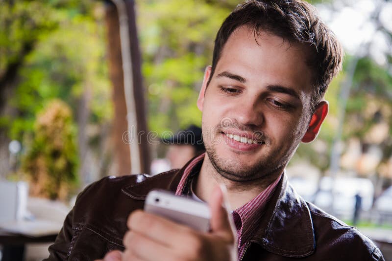 Happy Young Man Browsing Internet on Smartphone Sitting at Outdoor Cafe ...