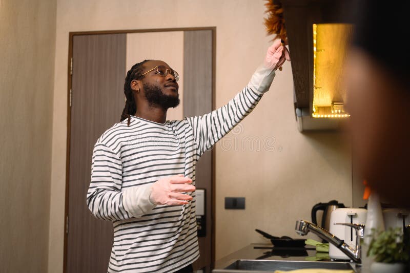 Happy Young Man Doing Chores Dusting Wooden Shelf with a Feather Duster ...