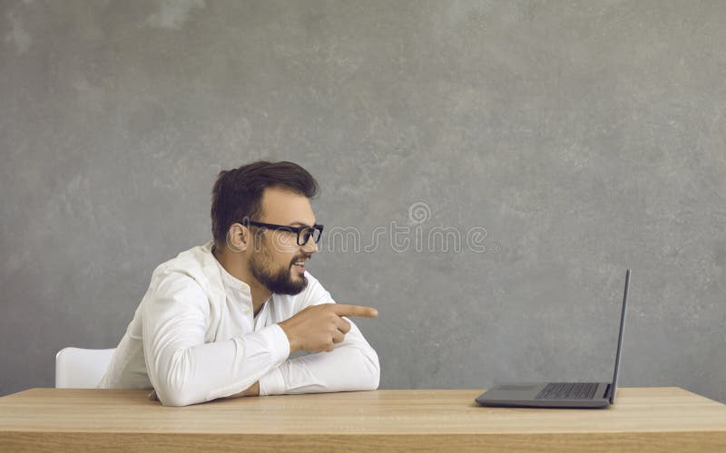 Happy Young Man Sitting at a Desk and Pointing at the Screen of a ...