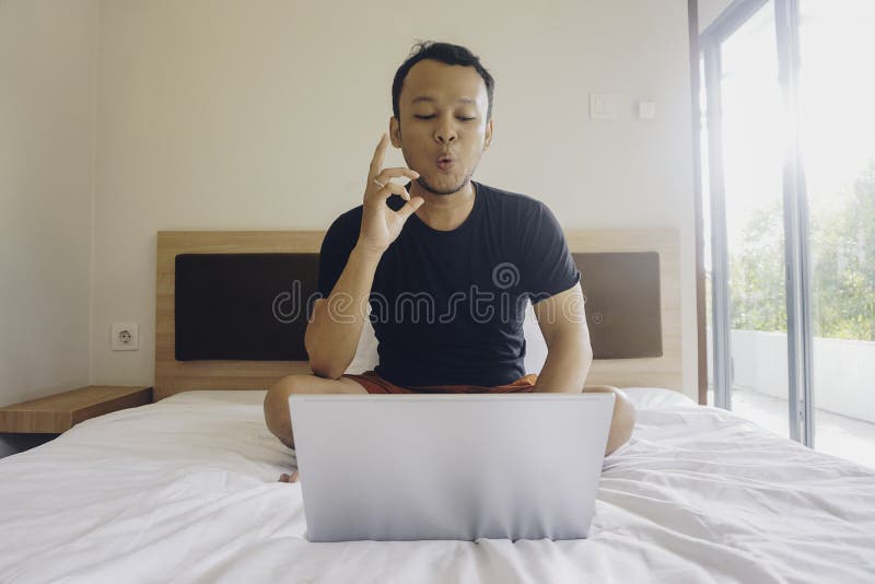 Happy Young Man Working from the Bed. Put the Laptop on the Bed and ...