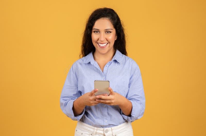 Happy Young Woman In A Blue Shirt Holding A Smartphone And Looking At