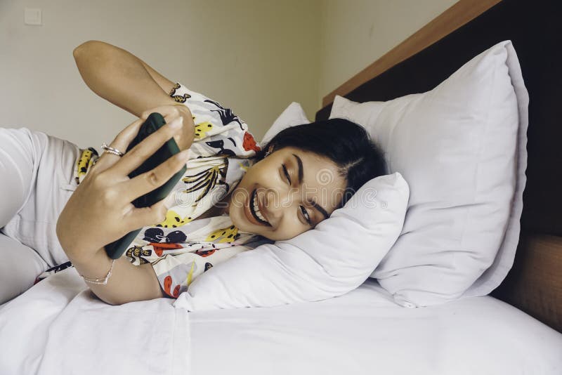 Happy Young Woman Checking on Her Phone while Lying in Bed Stock Photo ...