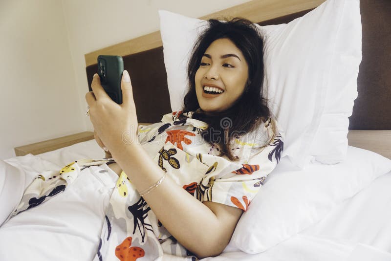 Happy Young Woman Checking on Her Phone while Lying in Bed Stock Photo ...