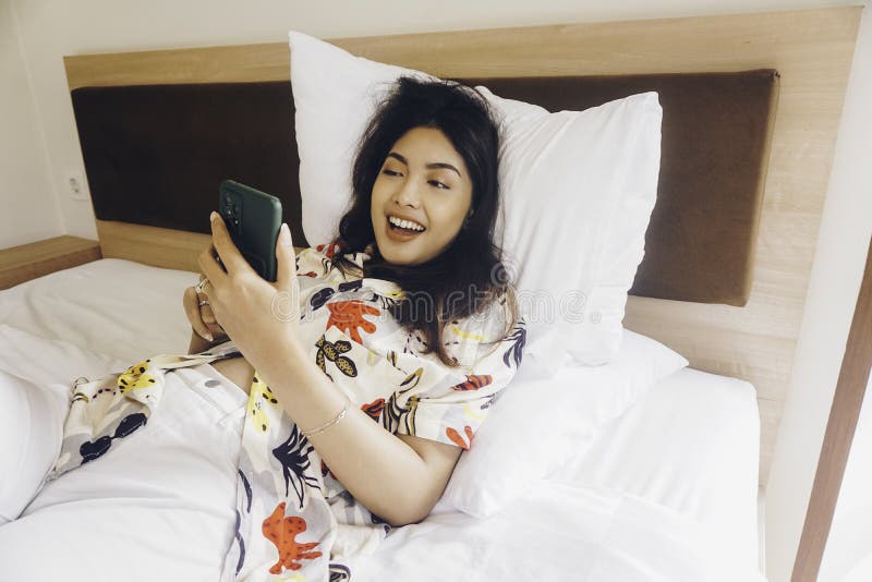 Happy Young Woman Checking on Her Phone while Lying in Bed Stock Photo ...